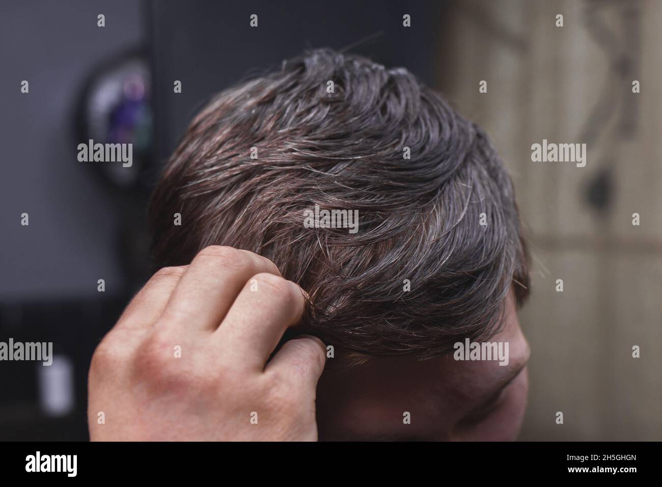 A man's hand touches his dark long hair necessary for a haircut and in ...