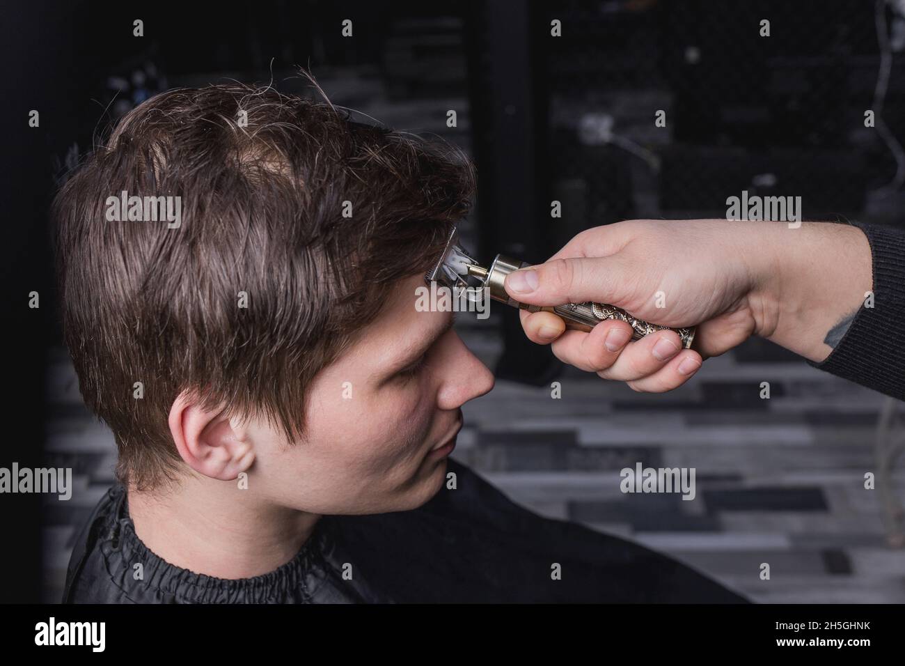 The hand of a barber or hairdresser with a portable clipper cuts the ...