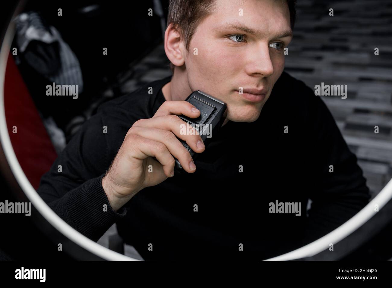 A serious young guy of Caucasian appearance with dark hair shaves with ...