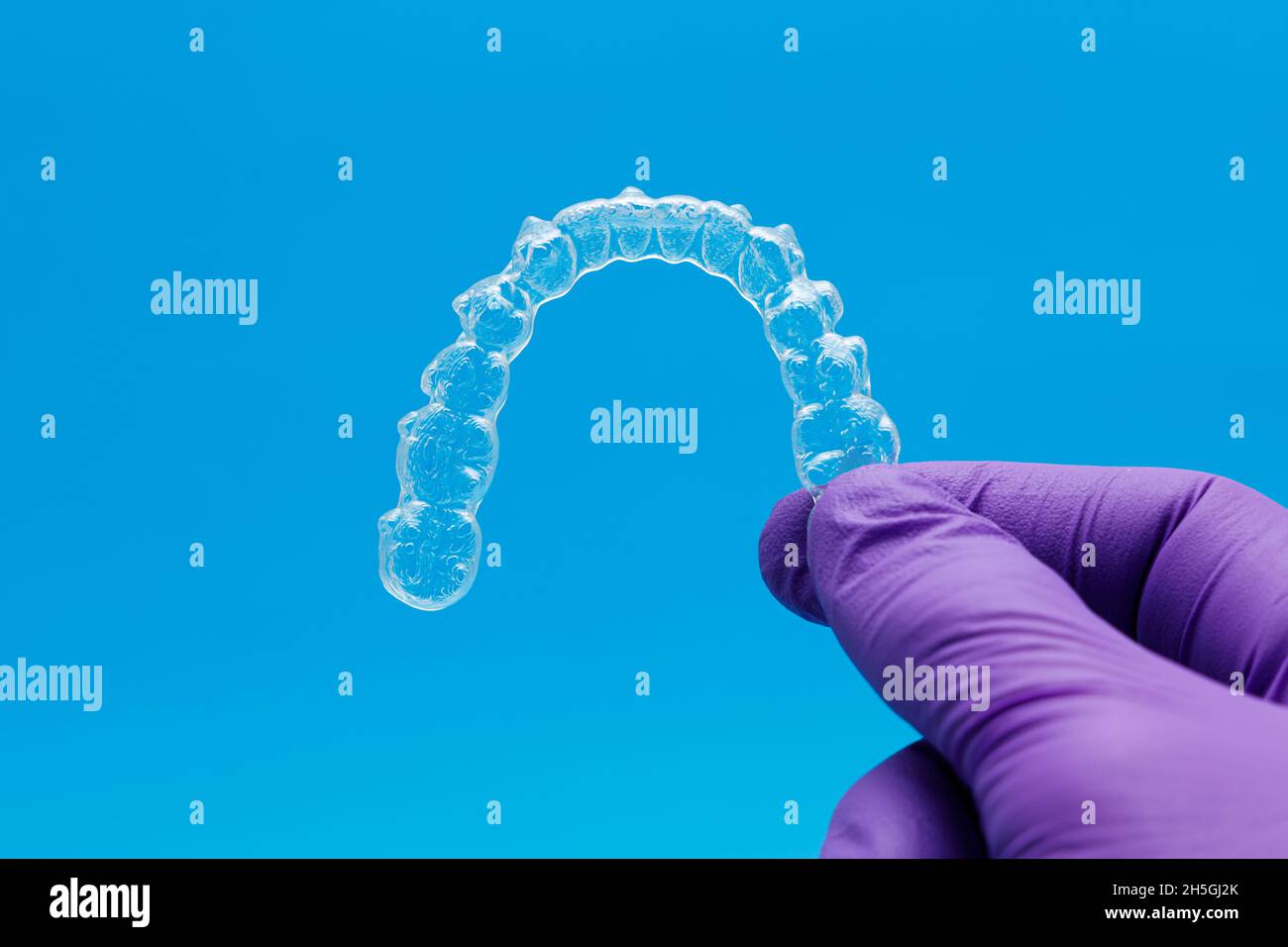 Hand holding one transparent retainer on blue background. Invisalign ...
