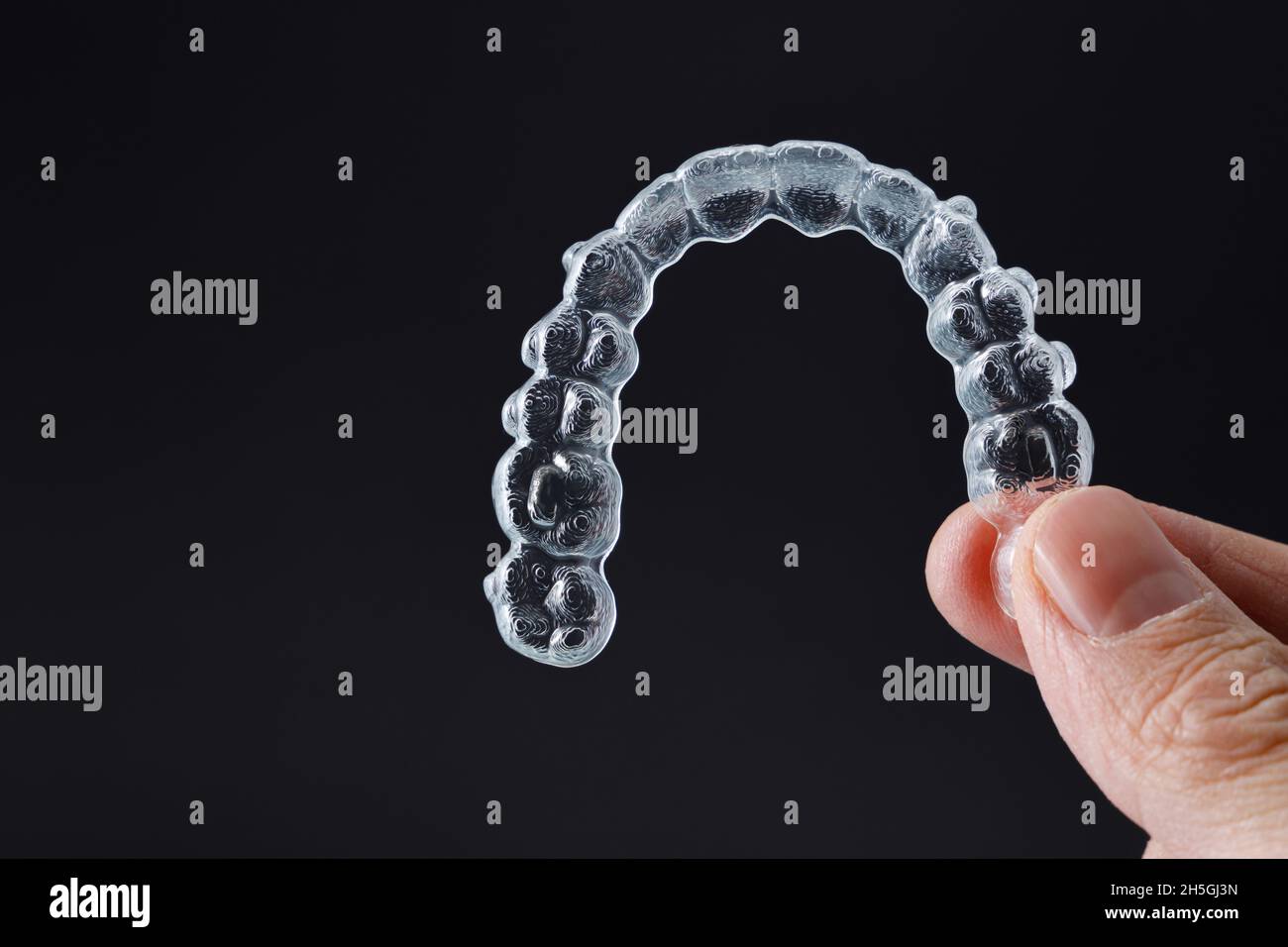 Hand holding one transparent retainer on black background. Invisalign ...