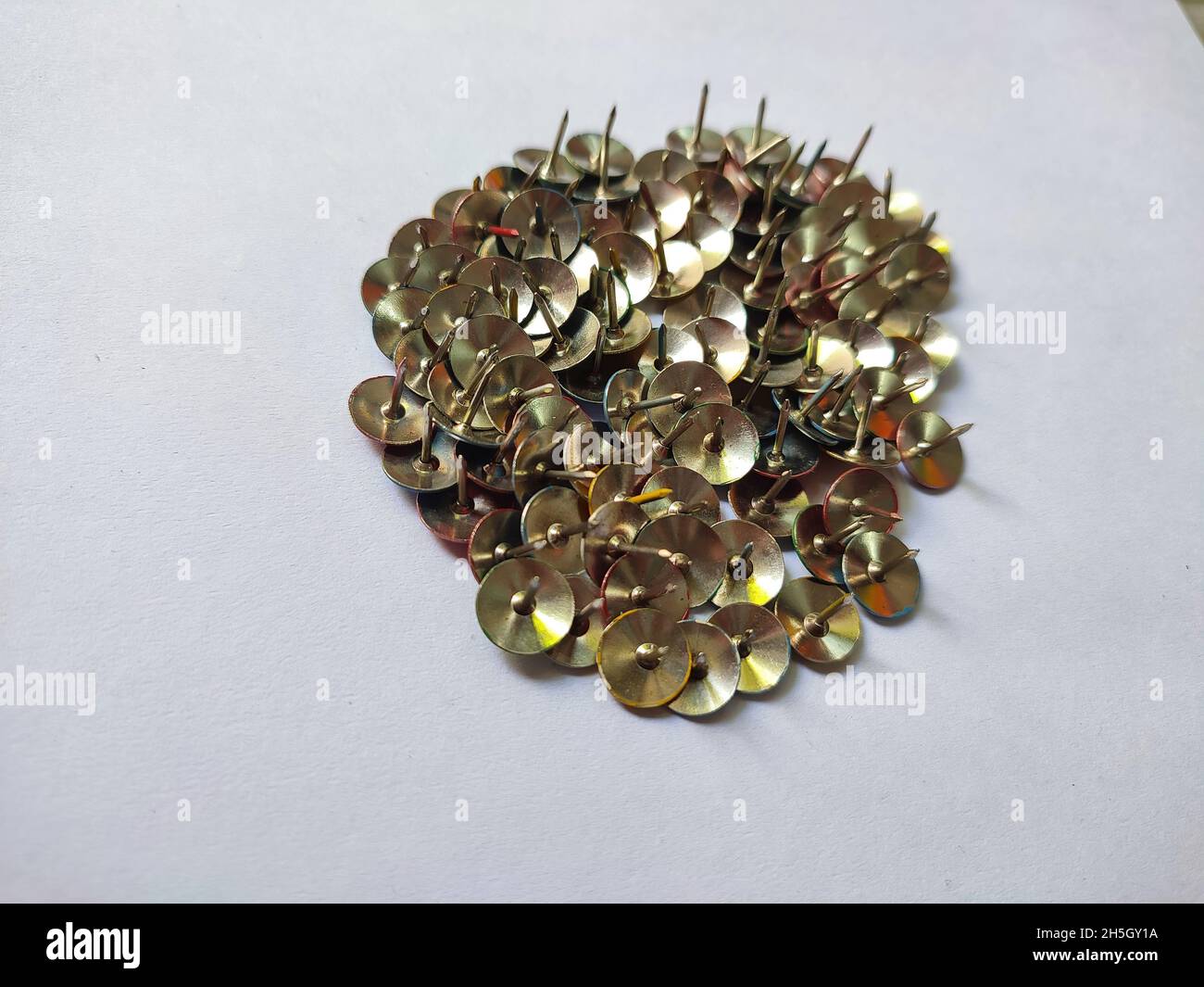 Pile of brass drawing pins on white background Stock Photo - Alamy
