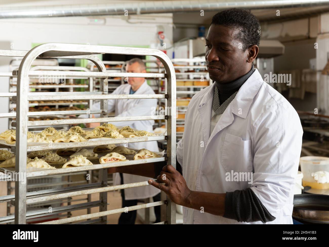 African baker carrying formed raw products on trolley Stock Photo - Alamy