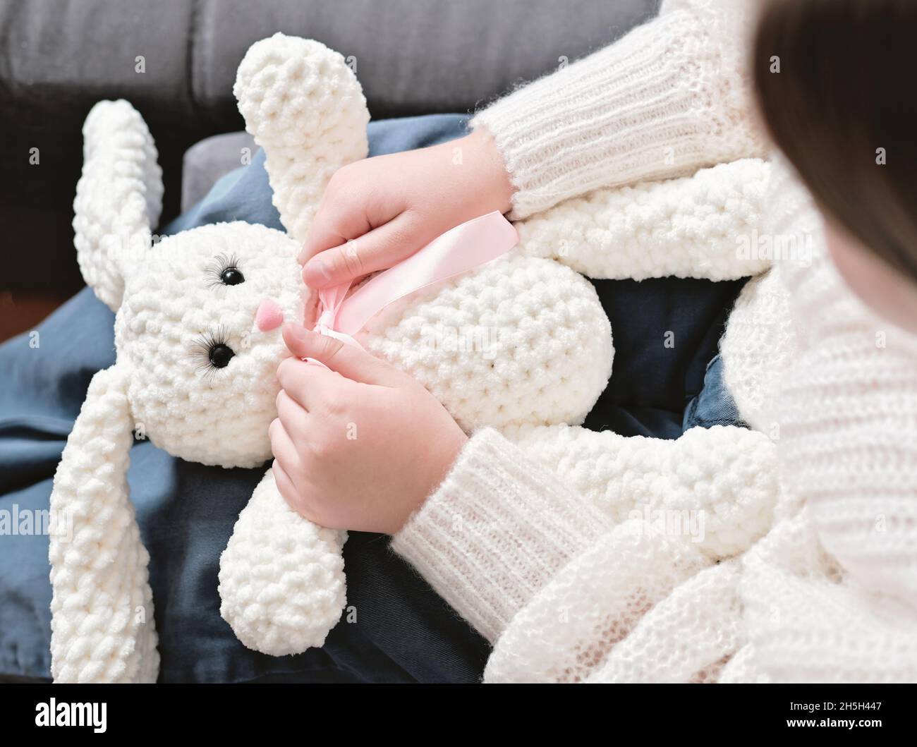 little girl playing with knitted rabbit and ties a ribbon or bow. Top ...