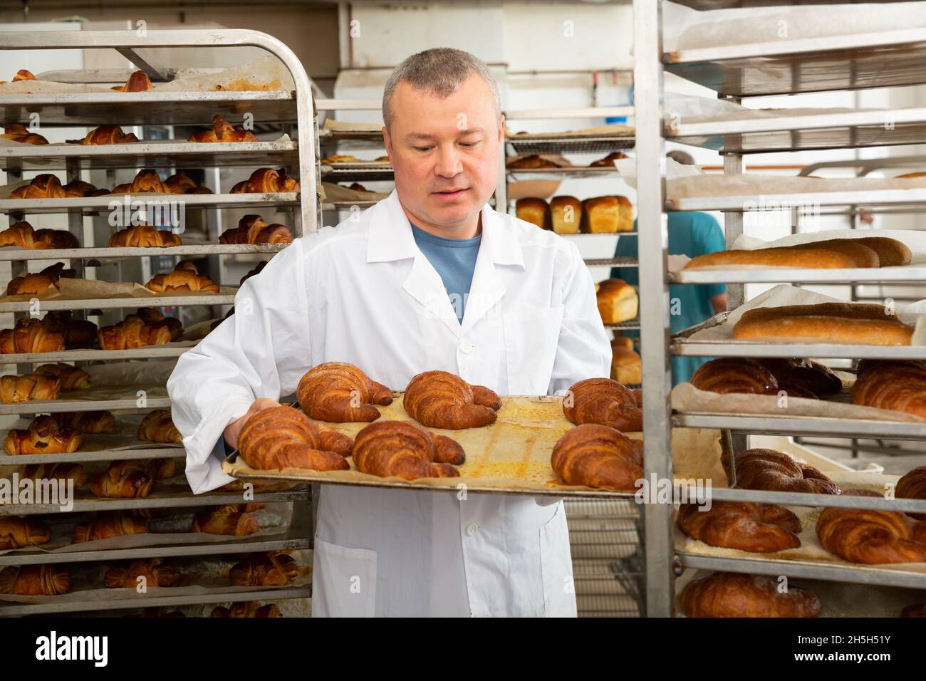 Baker putting baked bread on rack Stock Photo - Alamy