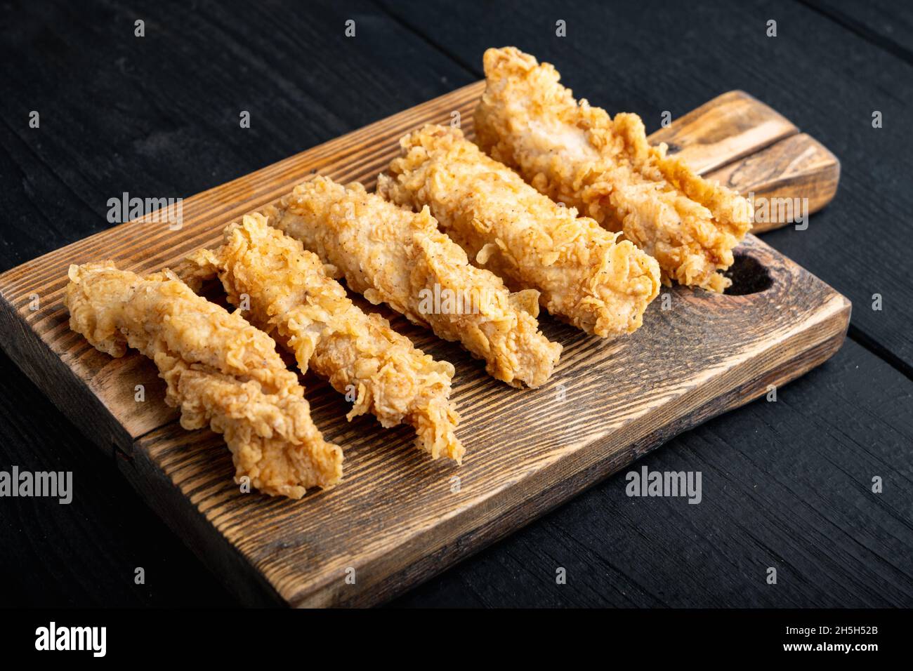 Chicken breaded fillet stripes on black wooden table Stock Photo - Alamy