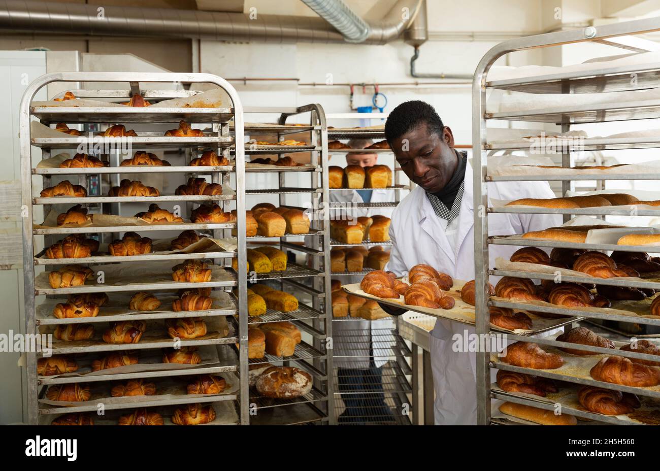 African baker putting tray with bakery goods on trolley Stock Photo - Alamy