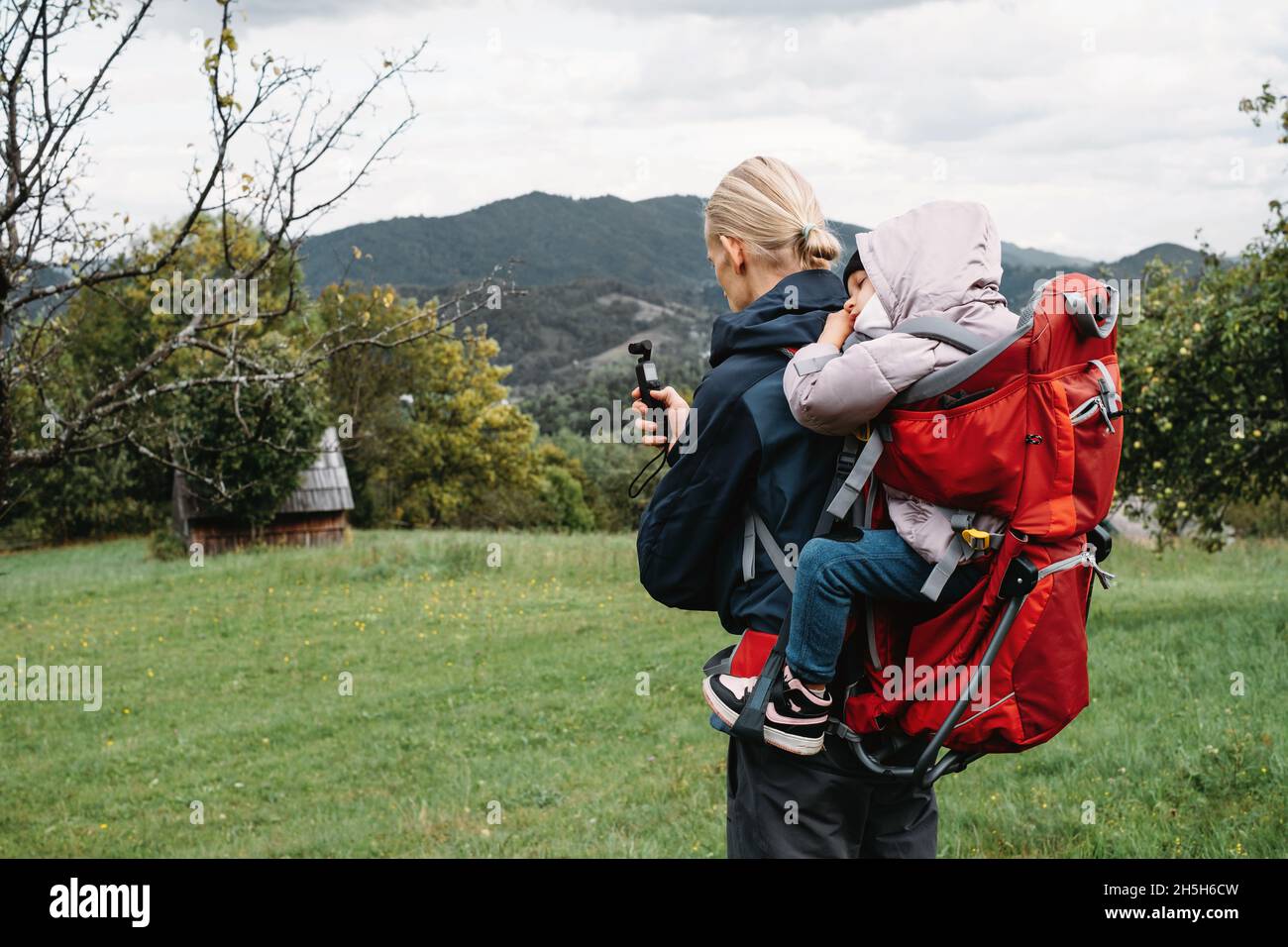 Father taking pictures while hiking with child in backpack. Vlogger man ...