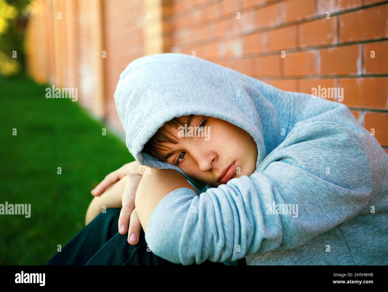 Sad Teenager sit by the Brick Wall outdoor Stock Photo - Alamy