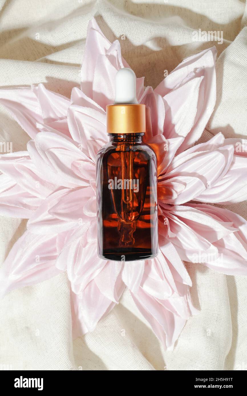 dark amber glass bottle with oil on flower and grey crumpled linen ...