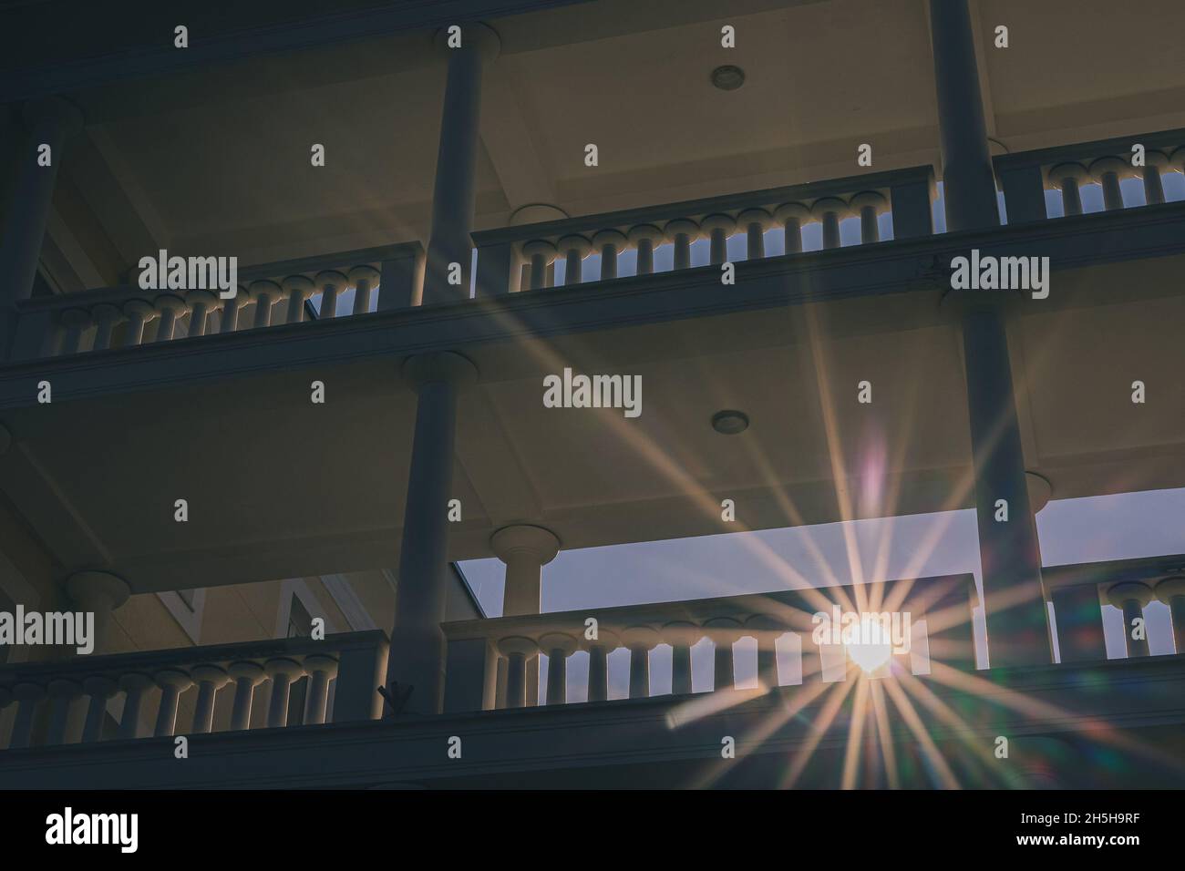 Sun with a lens flare poking out from a building filled with columns ...