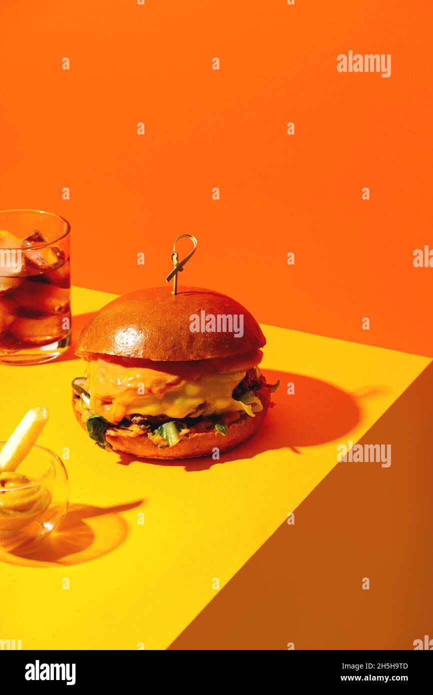 Big burger with french fries and sauce on bright orange and yellow ...