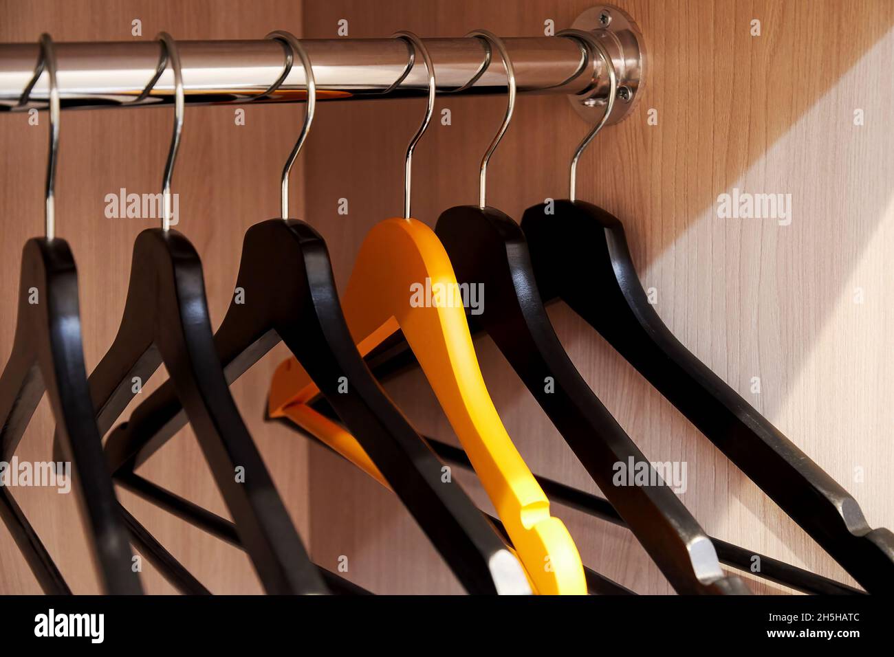 Set of black hangers in the wardrobe with one different orange hanger ...