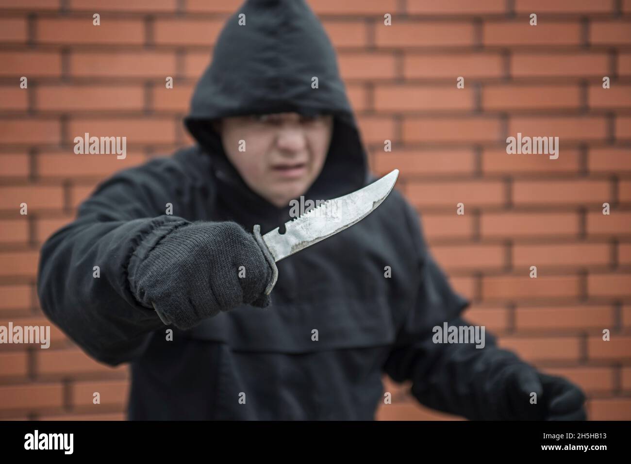 A man holding knife on brick background. The man with a knife in black ...