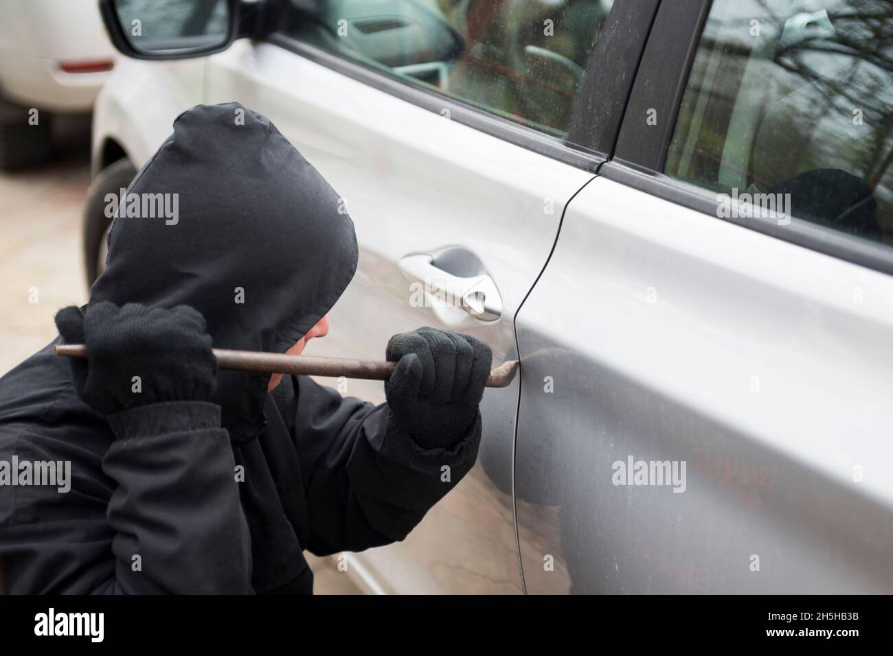 A robber dressed in black holding crowbar at a driver in a car. Car ...