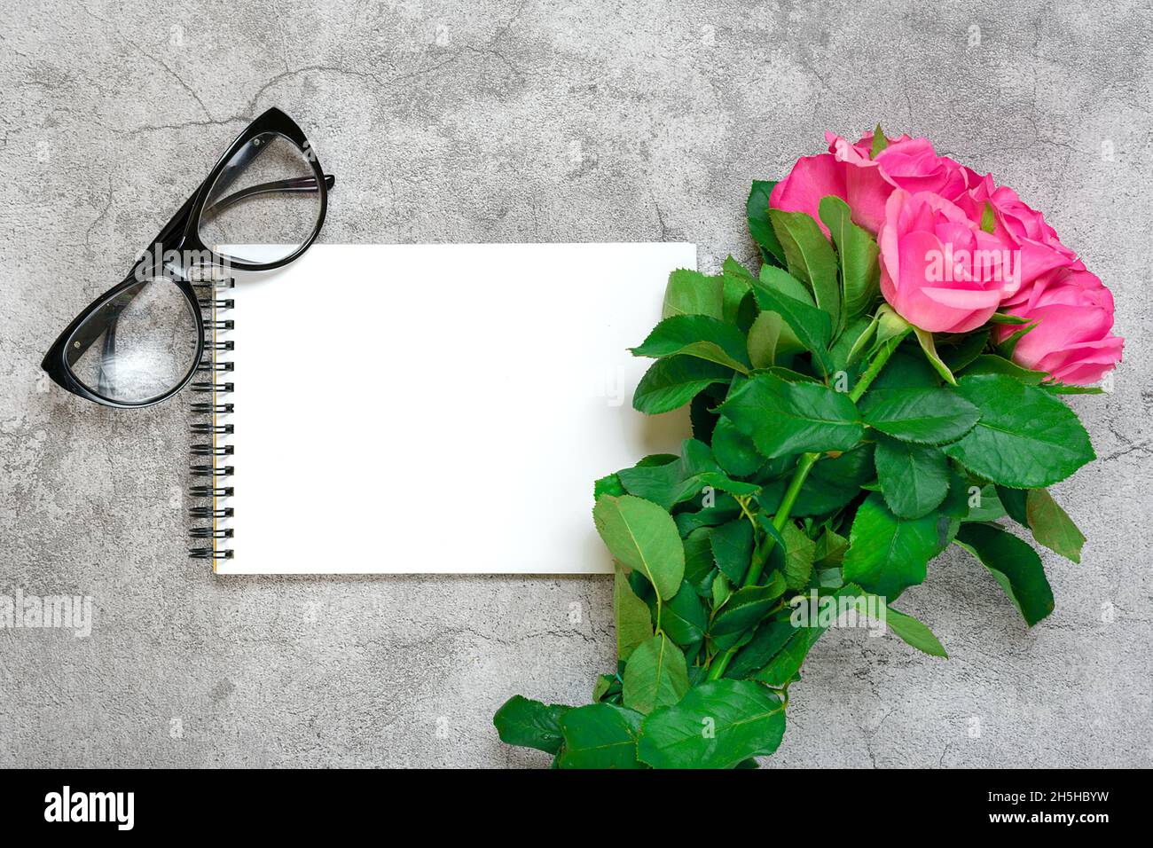 Beautiful pink roses flowers, white notepad, glass on concrete ...