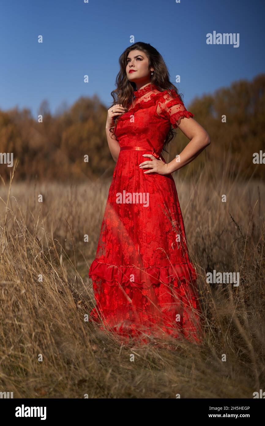 Woman in red dress in a meadow by the oak forest, November portrait ...