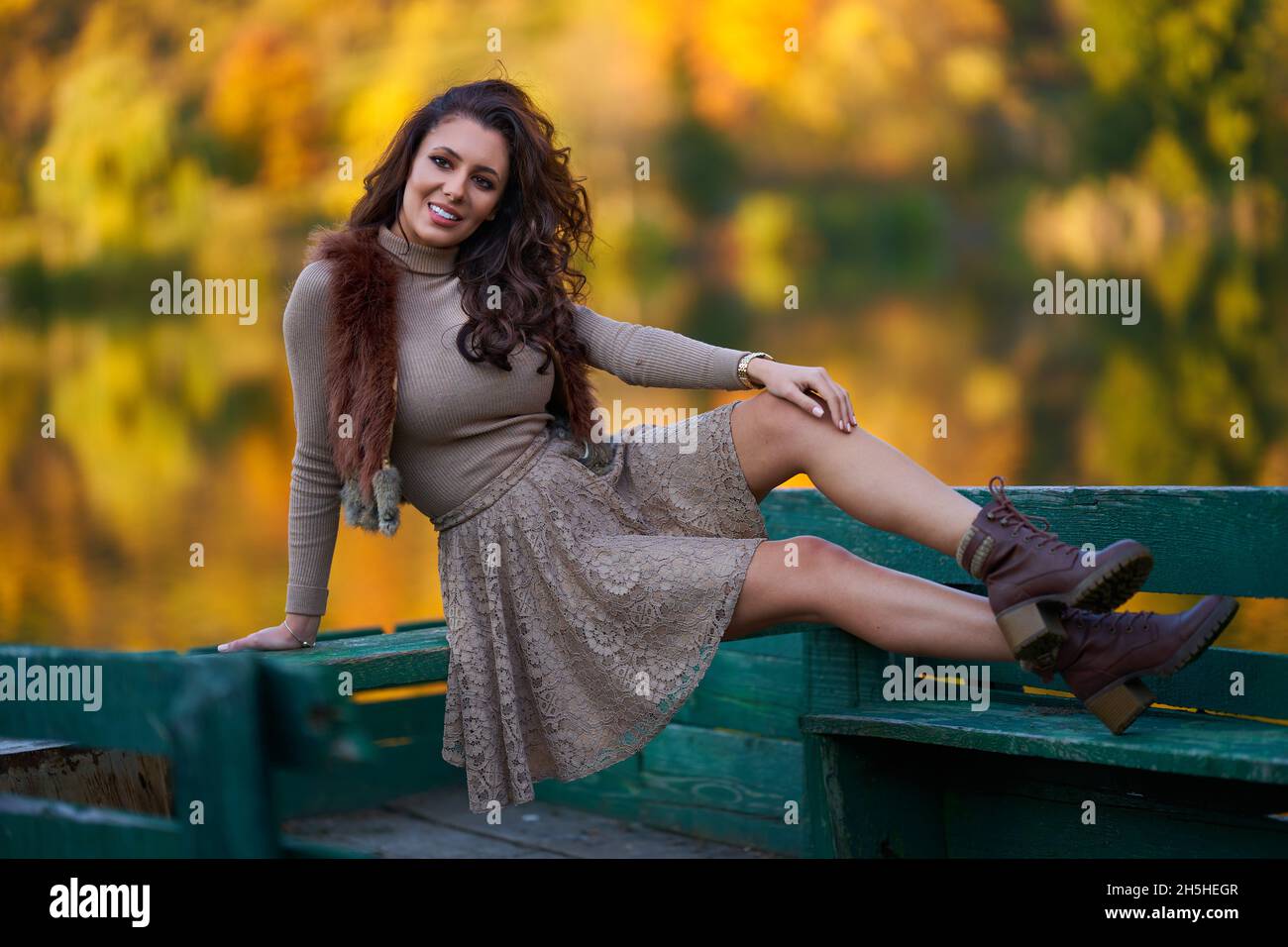 Beautiful fashion model sitting on a jetty leading into a lake ...