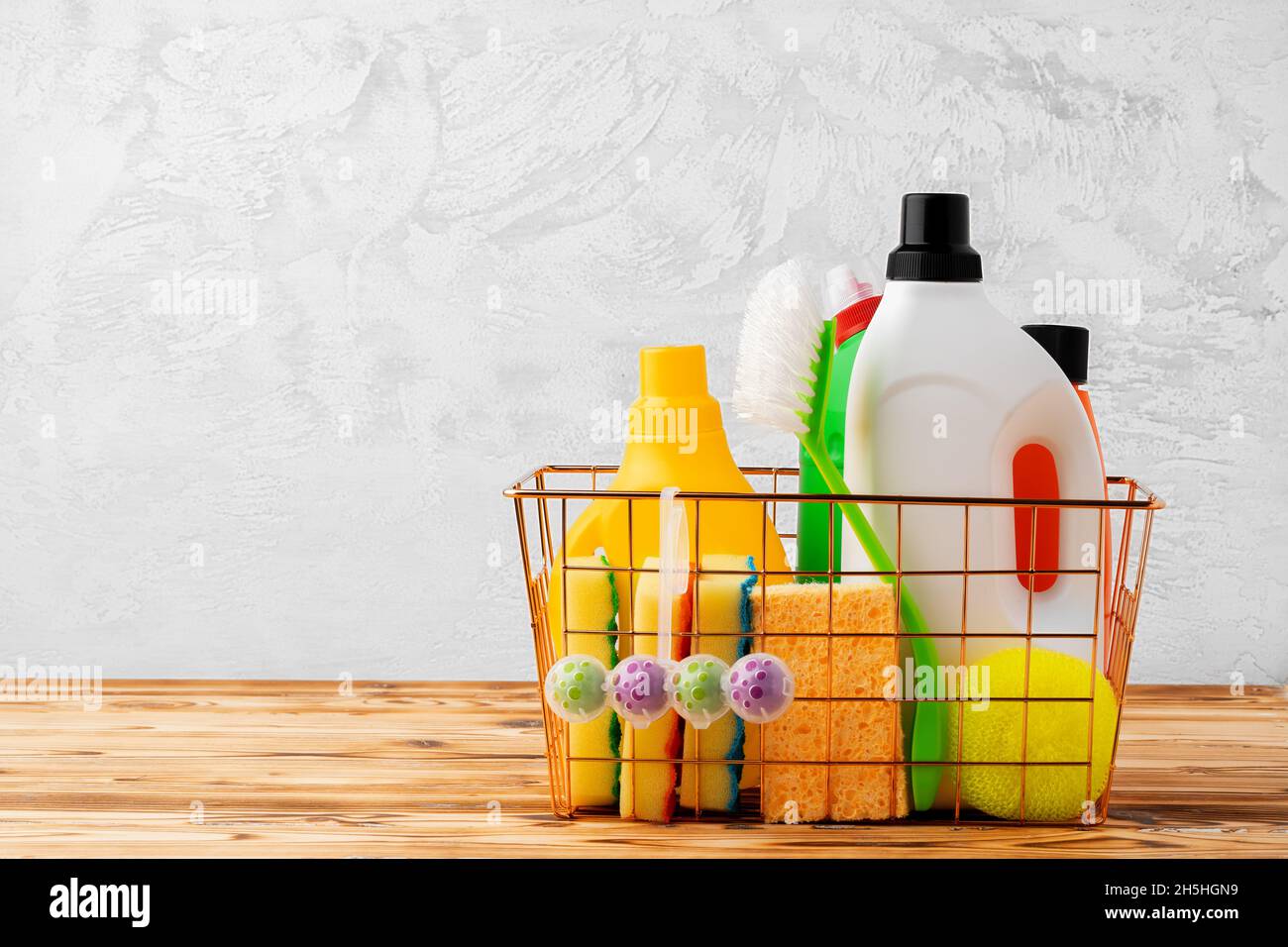 Cleaning tools and chemicals in basket on wooden table against gray ...