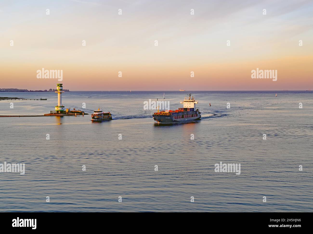 Cargo ship and passenger ferry in the Kiel Fjord at sunset, lighthouse ...