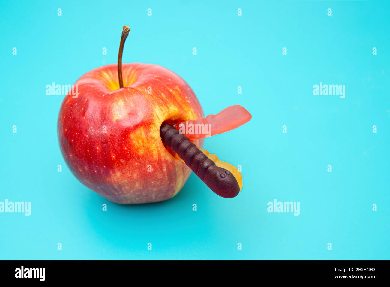 Candy worms in red apple on blue background Stock Photo - Alamy