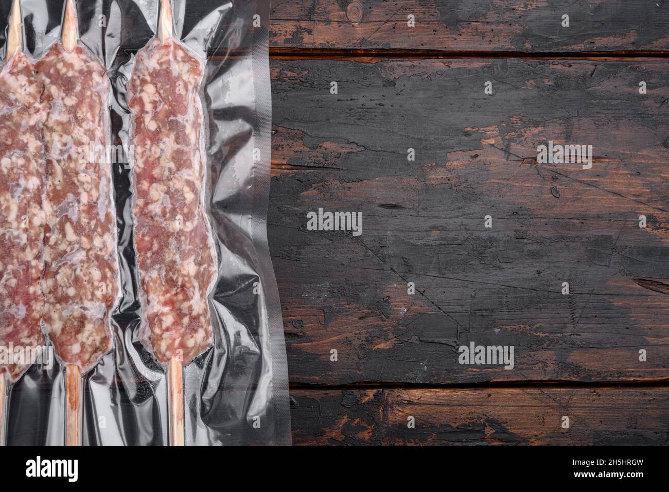 Mutton minced meat on skewers in vacuum pack set, on old dark wooden ...