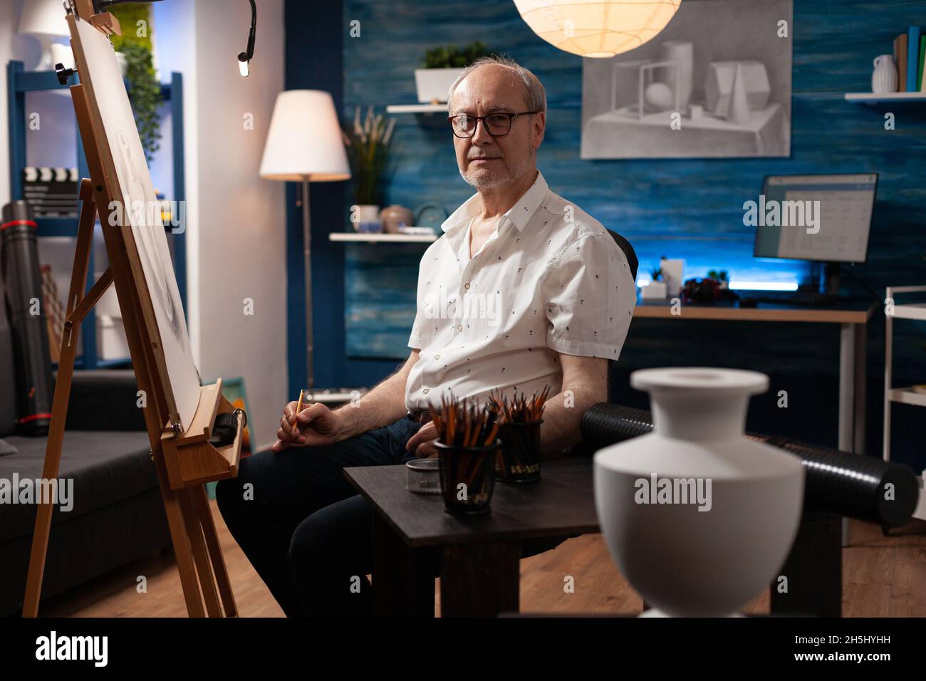 Senior artist looking at camera sitting in workshop at art studio ...