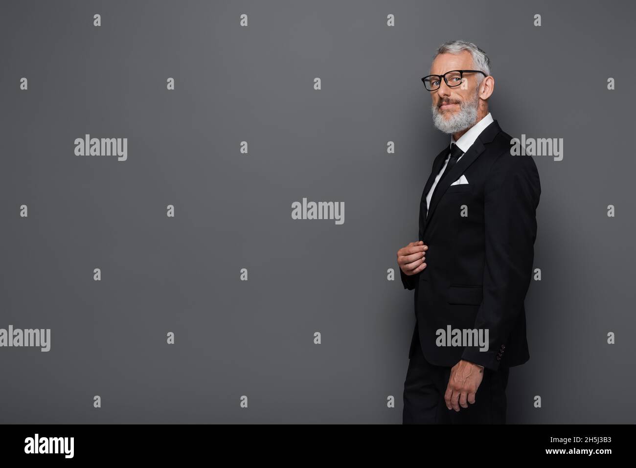 pleased middle aged businessman in glasses and suit isolated on grey ...