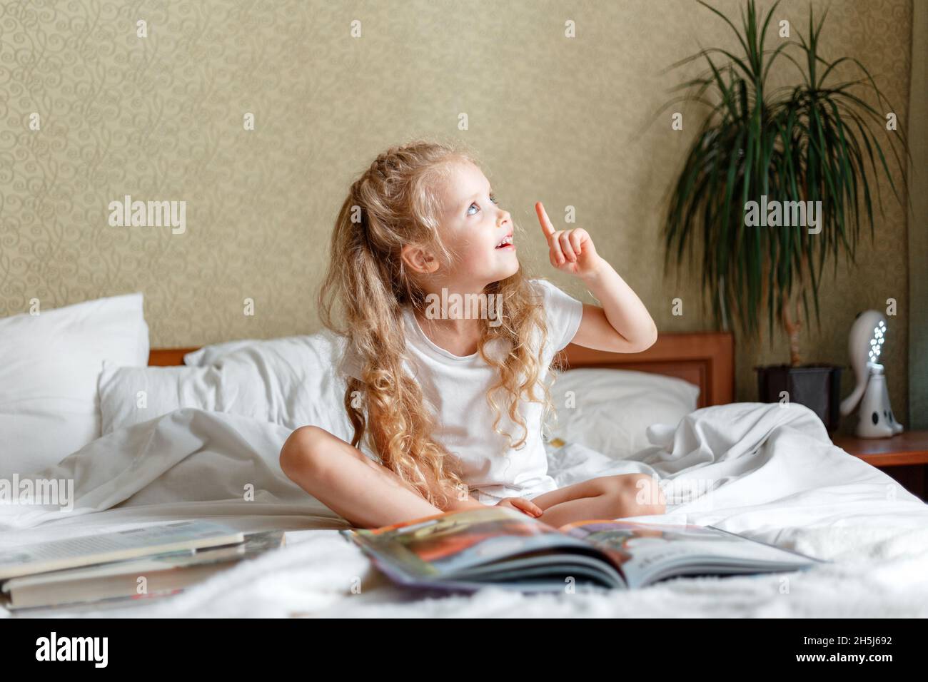 Clever beautiful little child girl pointing up by finger while reading ...