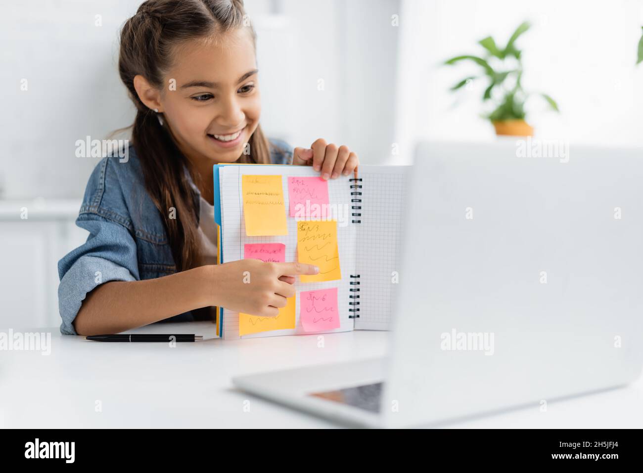 Smiling child pointing at sticky notes on notebook near laptop during ...