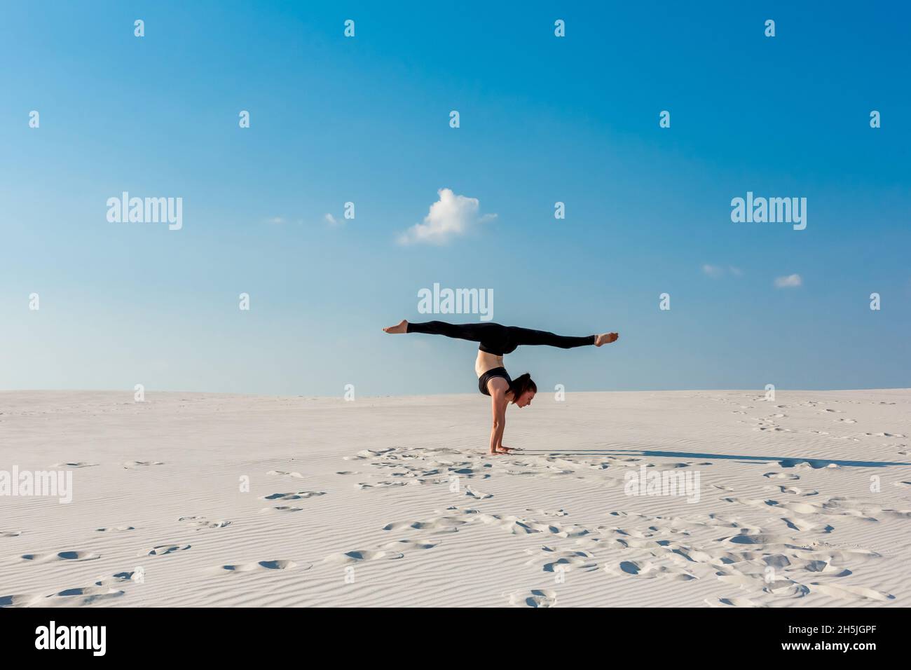 Young woman practicing handstand on beach with white sand and bright ...
