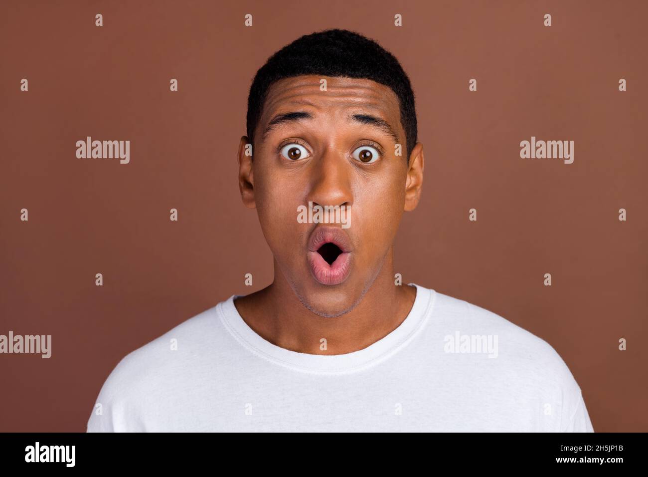 Photo of young african guy astonished crazy open mouth staring fake news isolated over brown ...