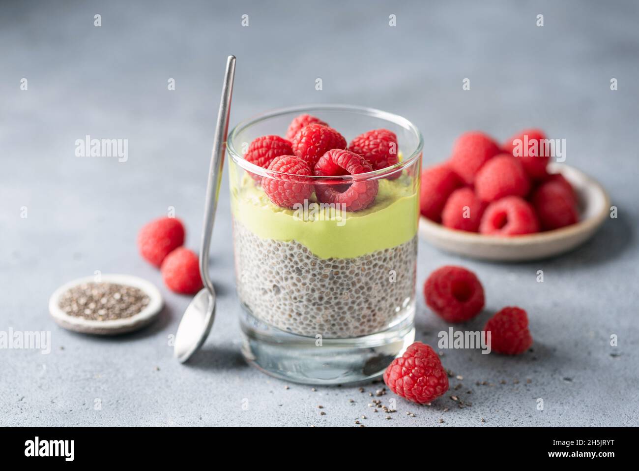 Chia seed pudding with avocado and raspberries in glass jar, closeup ...