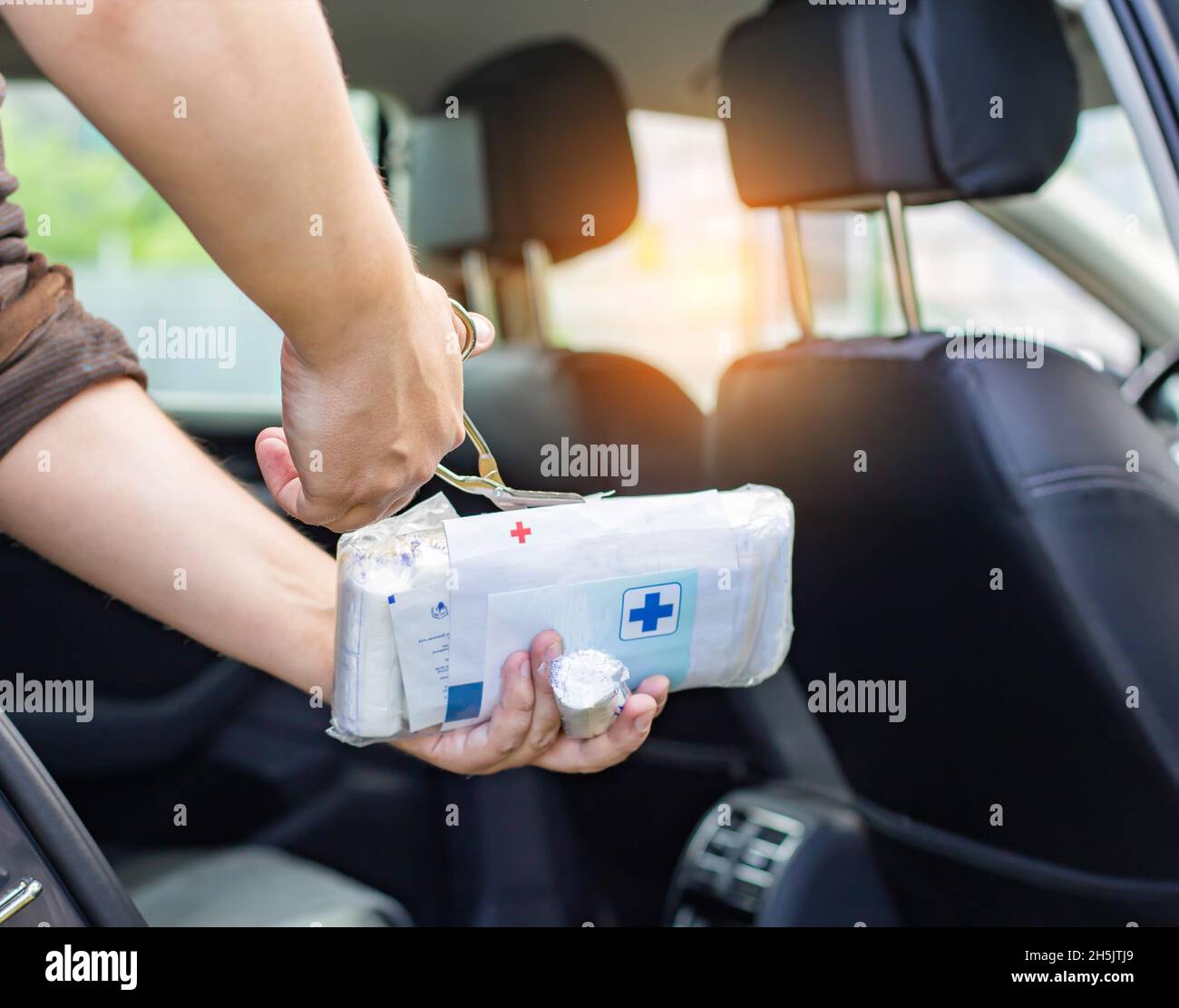 a man opens a bandage in a car first aid kit with scissors. Accident ...