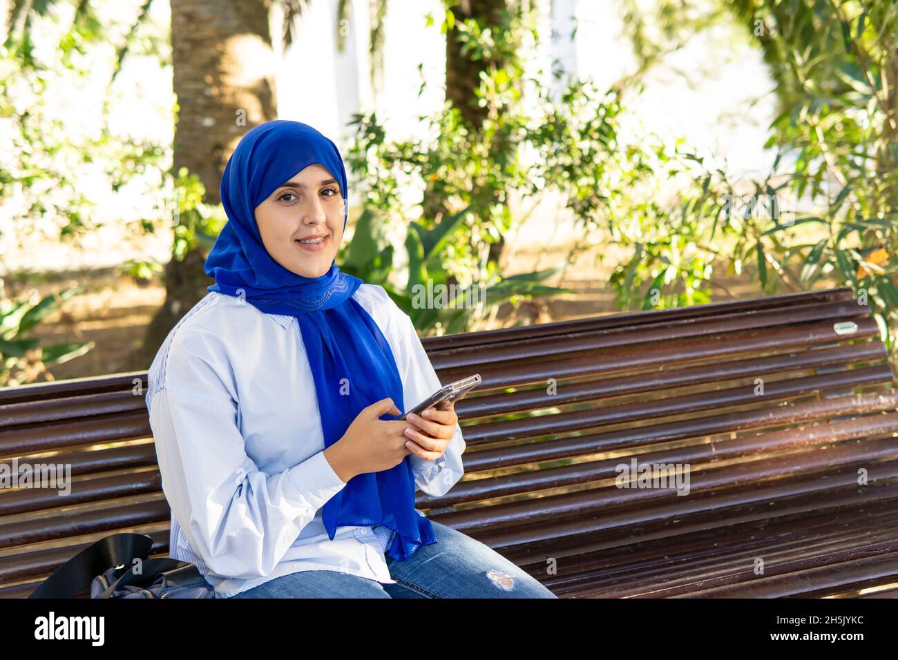 Young Muslim woman wearing hijab sitting on park bench using the Stock ...