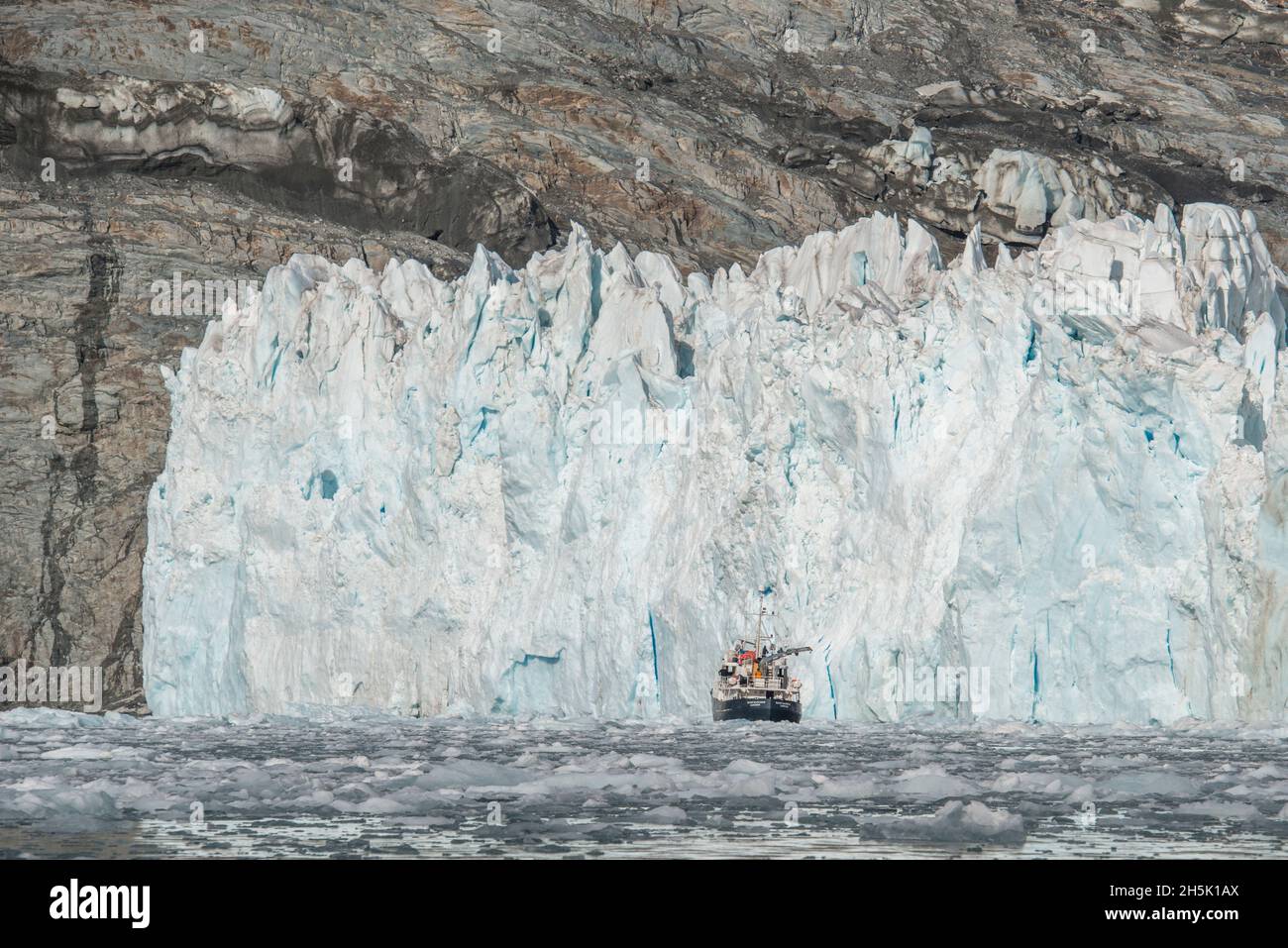 Ship in front of the icy wall of a tidewater glacier at the shore of ...