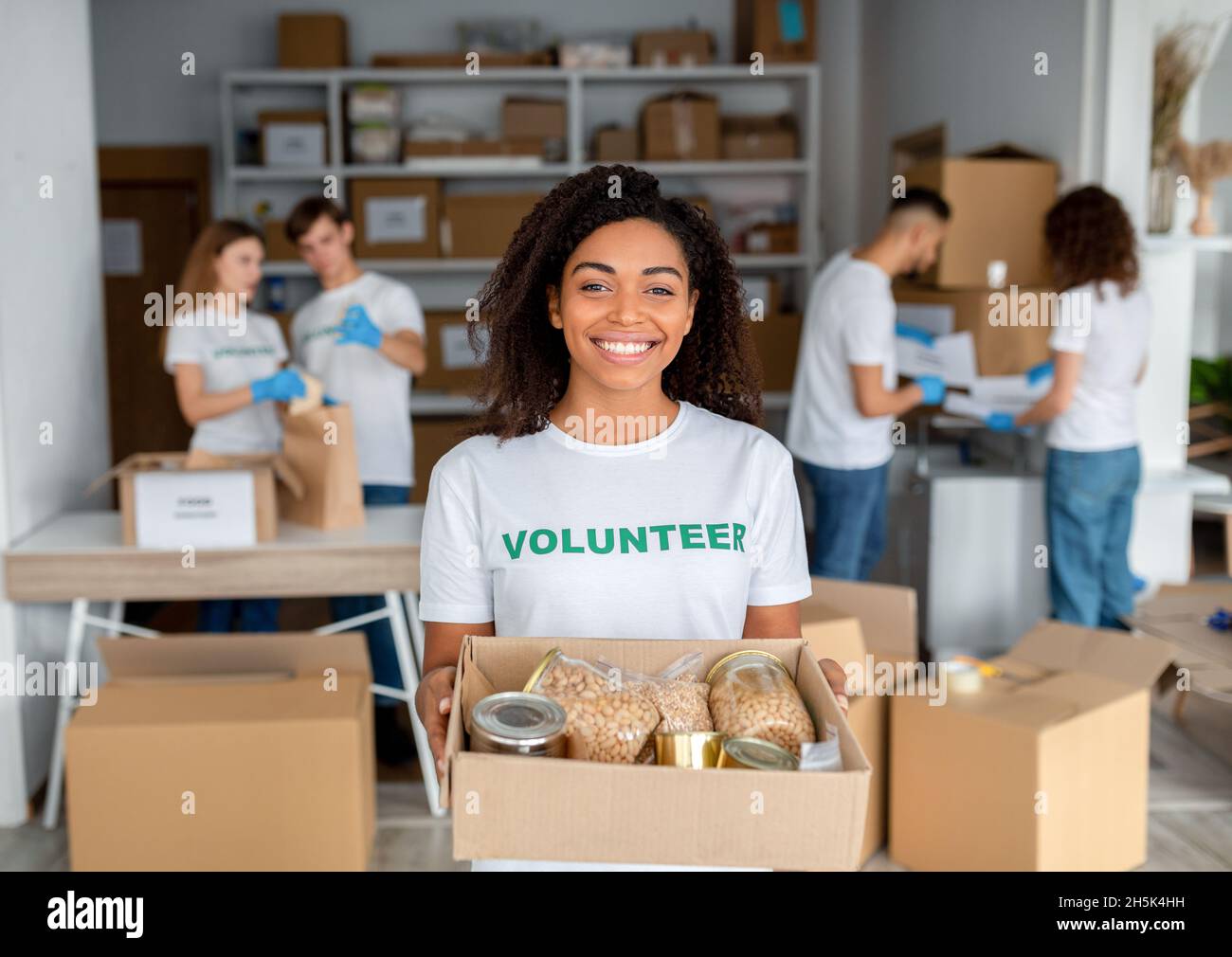 Young black female volunteer holding food donation box and smiling to ...