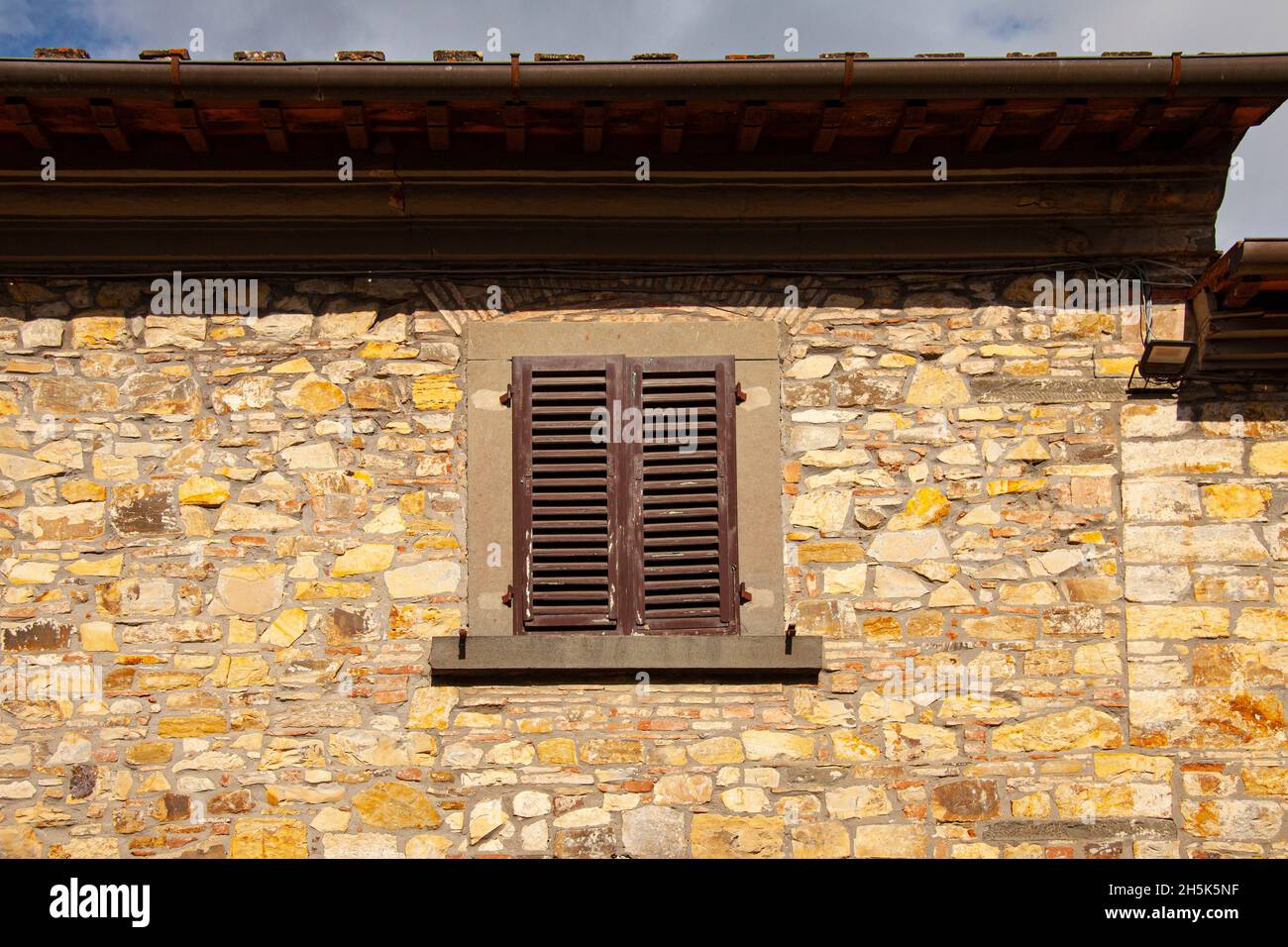 Brown shutters on the window against a rustic stone wall. Old exterior ...