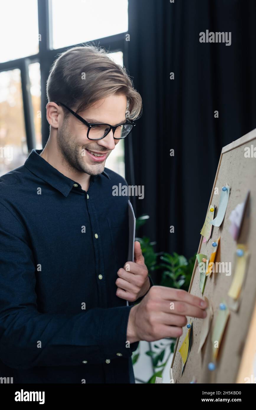 Positive developer with paper folder looking at sticky notes on board ...