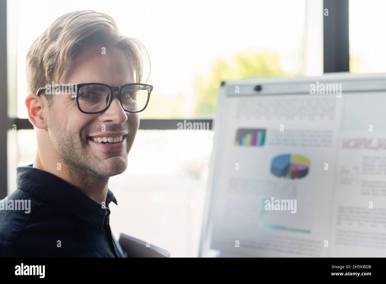 Smiling programmer in eyeglasses looking at camera near blurred flip ...