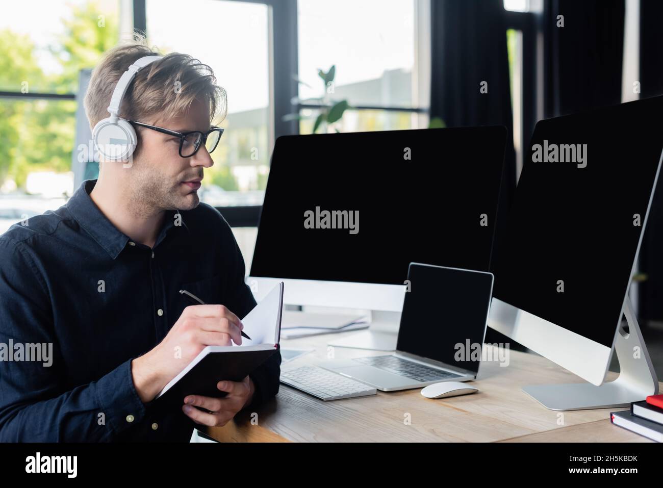 Programmer in headphones holding notebook near computers in office ...