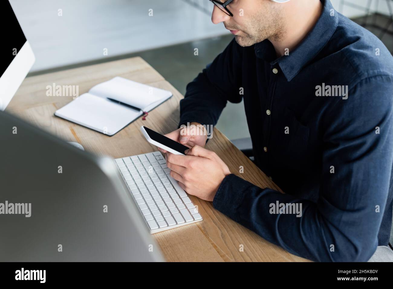 Cropped view of programmer using smartphone near computers and notebook ...