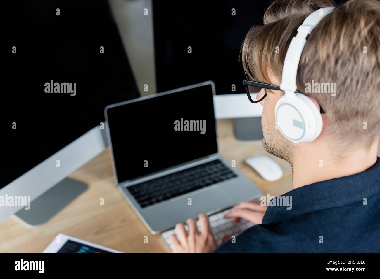 Programmer in headphones using blurred computers near laptop Stock ...