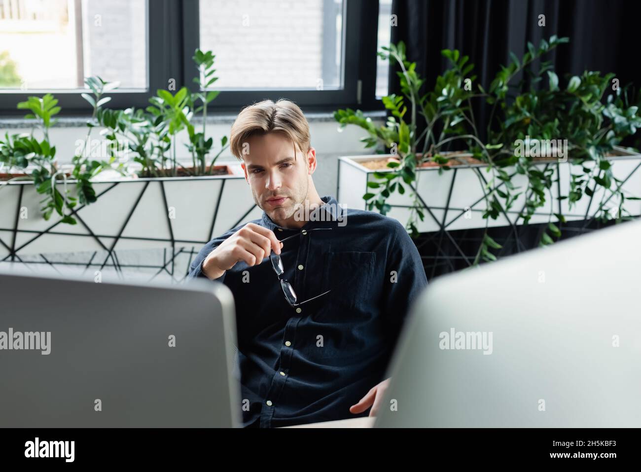 Programmer holding eyeglasses near blurred computer monitors Stock Photo - Alamy