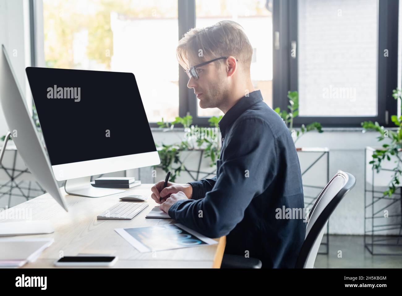 Side view of developer writing on notebook near computers with blank ...