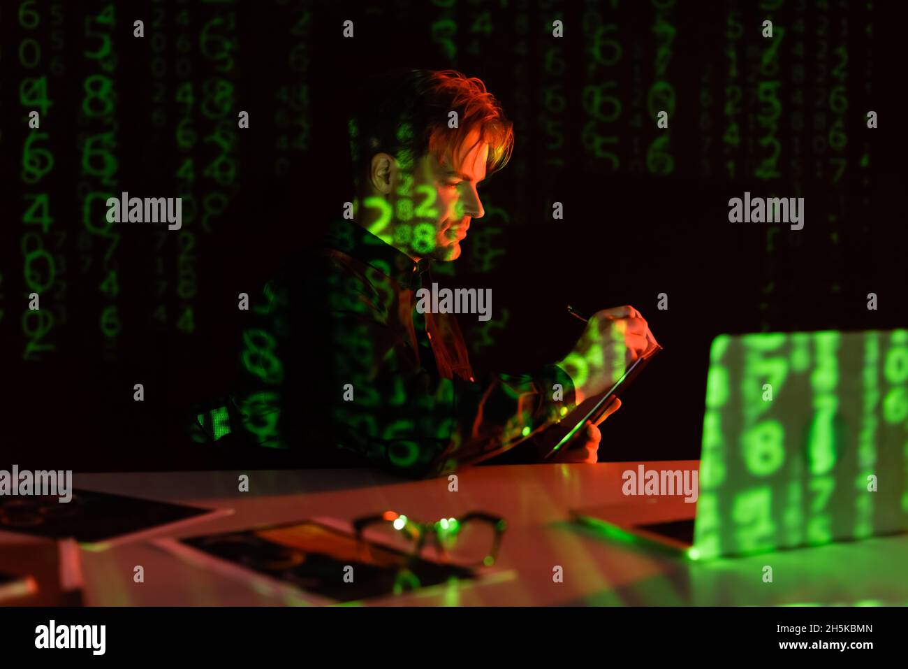 Side view of programmer writing on clipboard near laptop with ...