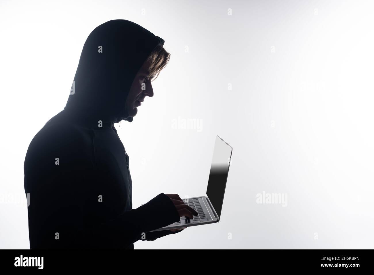 Side view of hacker in hood using laptop with blank screen isolated on ...