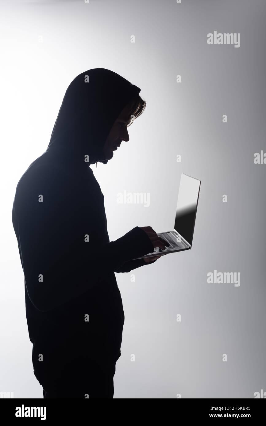 Side view of hacker in hood using laptop isolated on grey Stock Photo ...