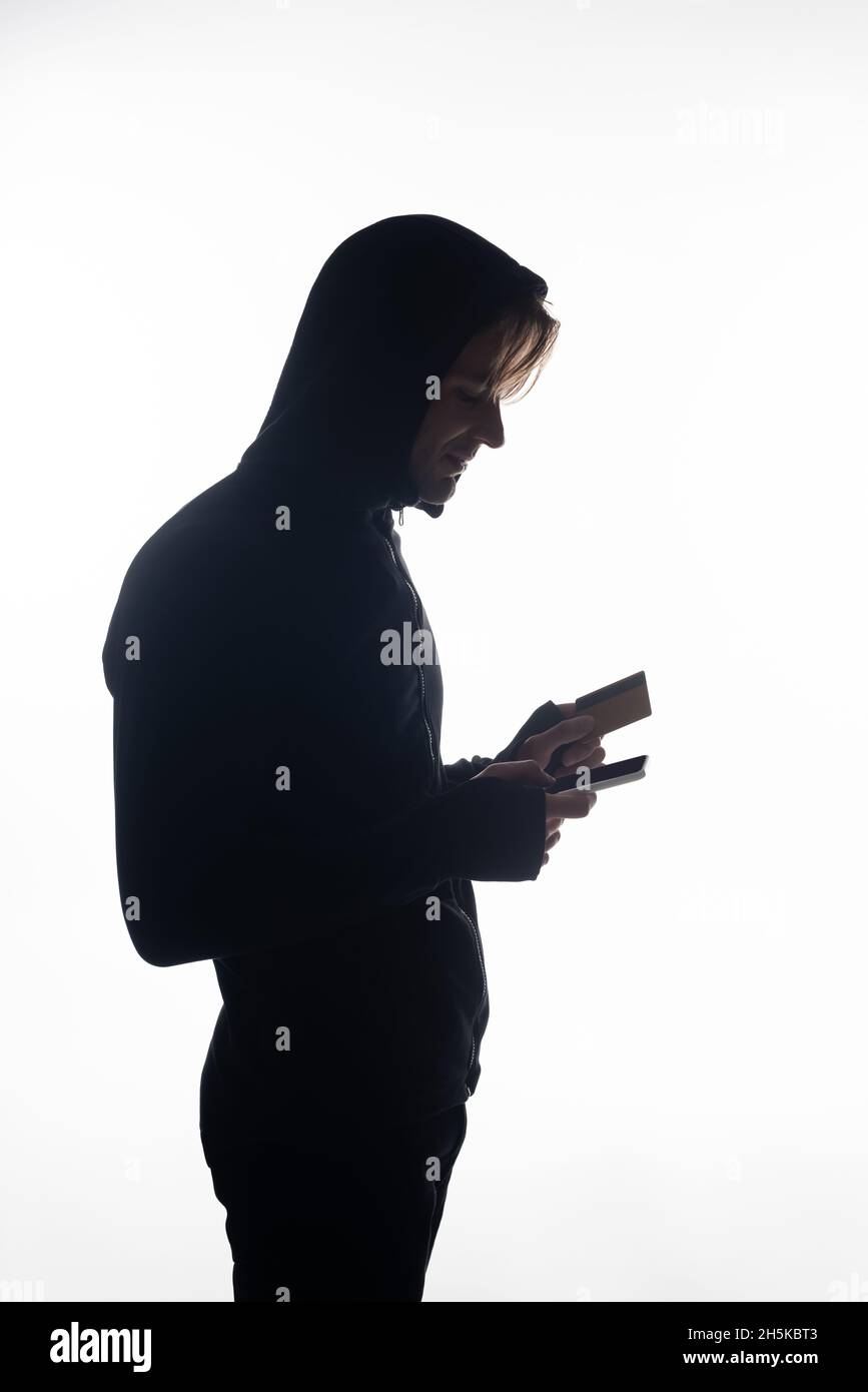 Side view of hacker holding cellphone and credit card isolated on white ...
