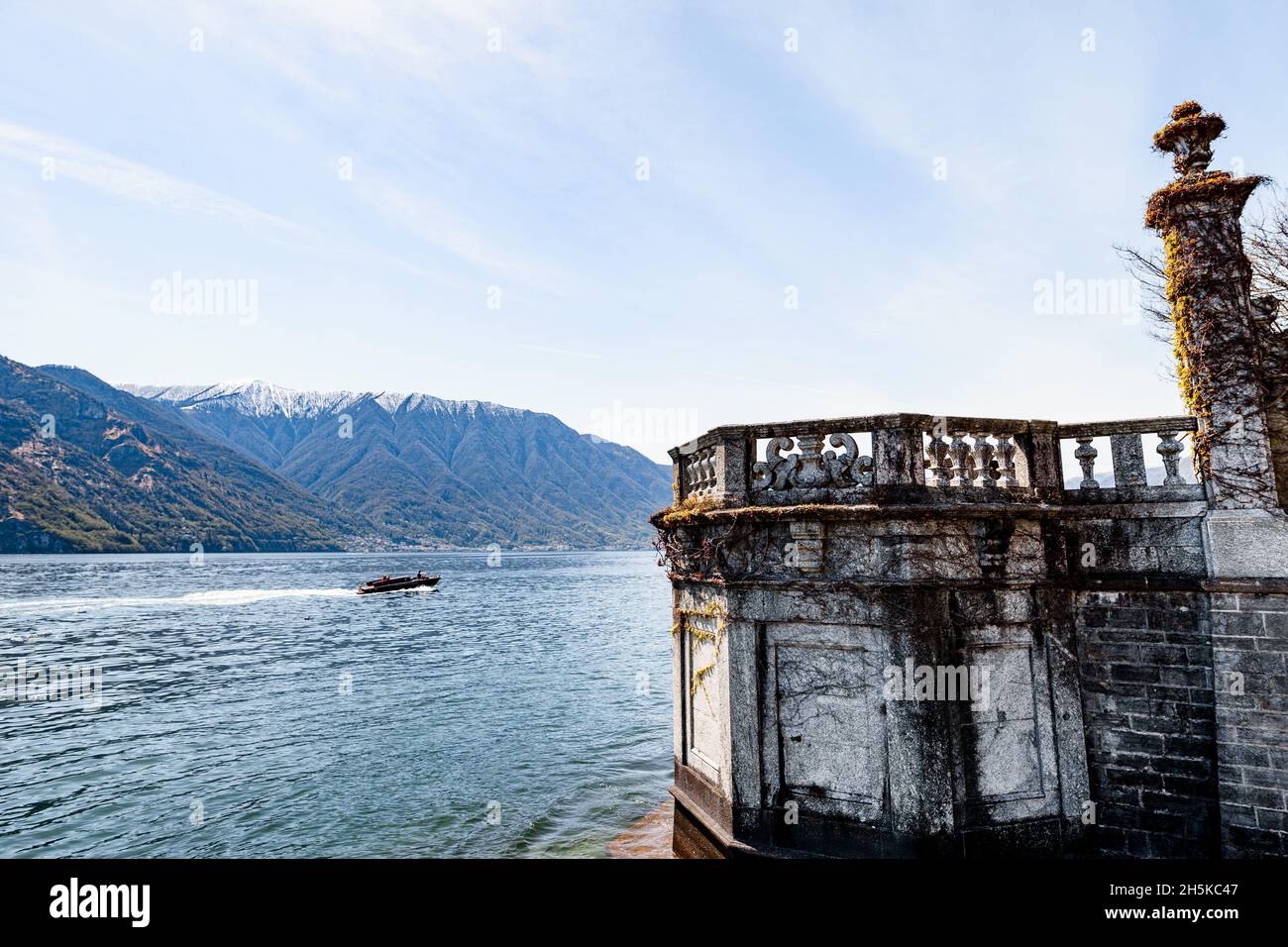 Yacht sails on Lake Como against the backdrop of a stone fence with a ...